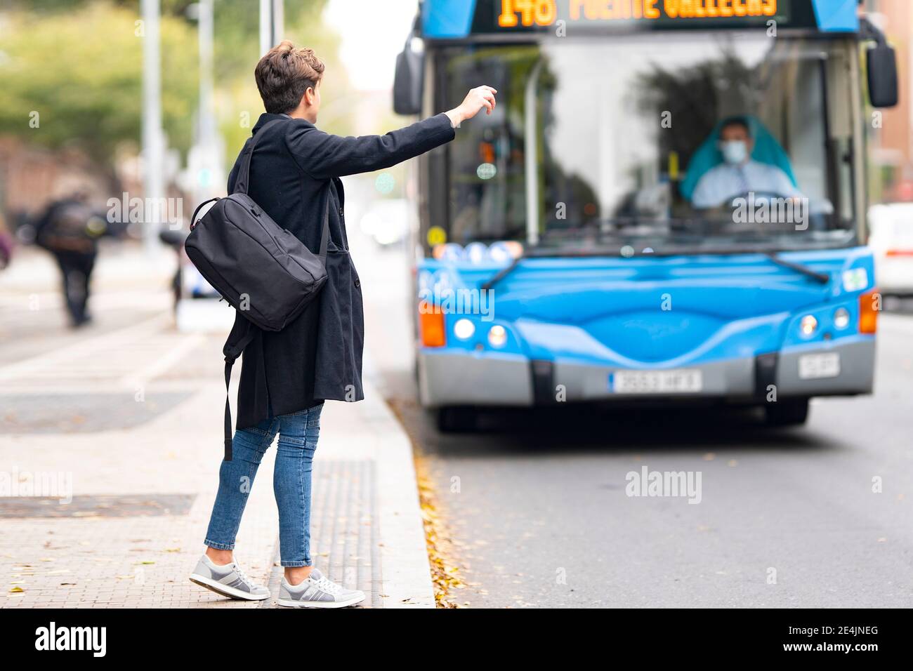 Young man hailing bus from footpath in city Stock Photo - Alamy