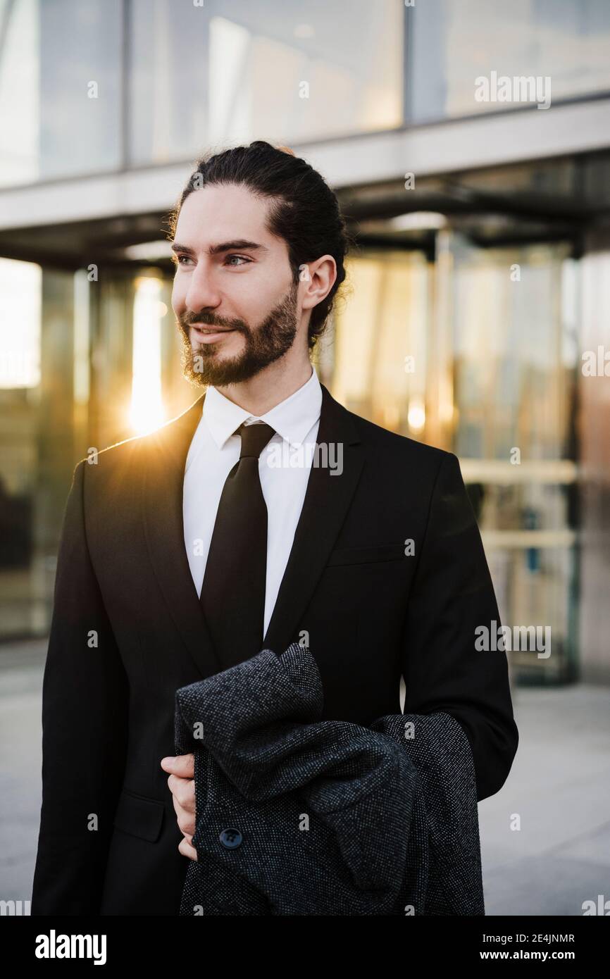 Smiling businessman holding jacket while standing outdoors Stock Photo ...