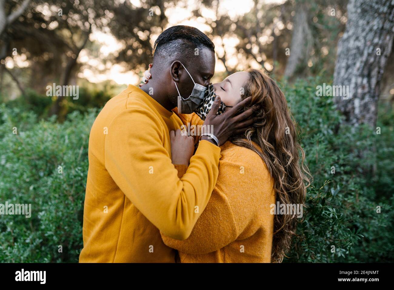 Couple wearing protective face mask kissing while standing at forest ...
