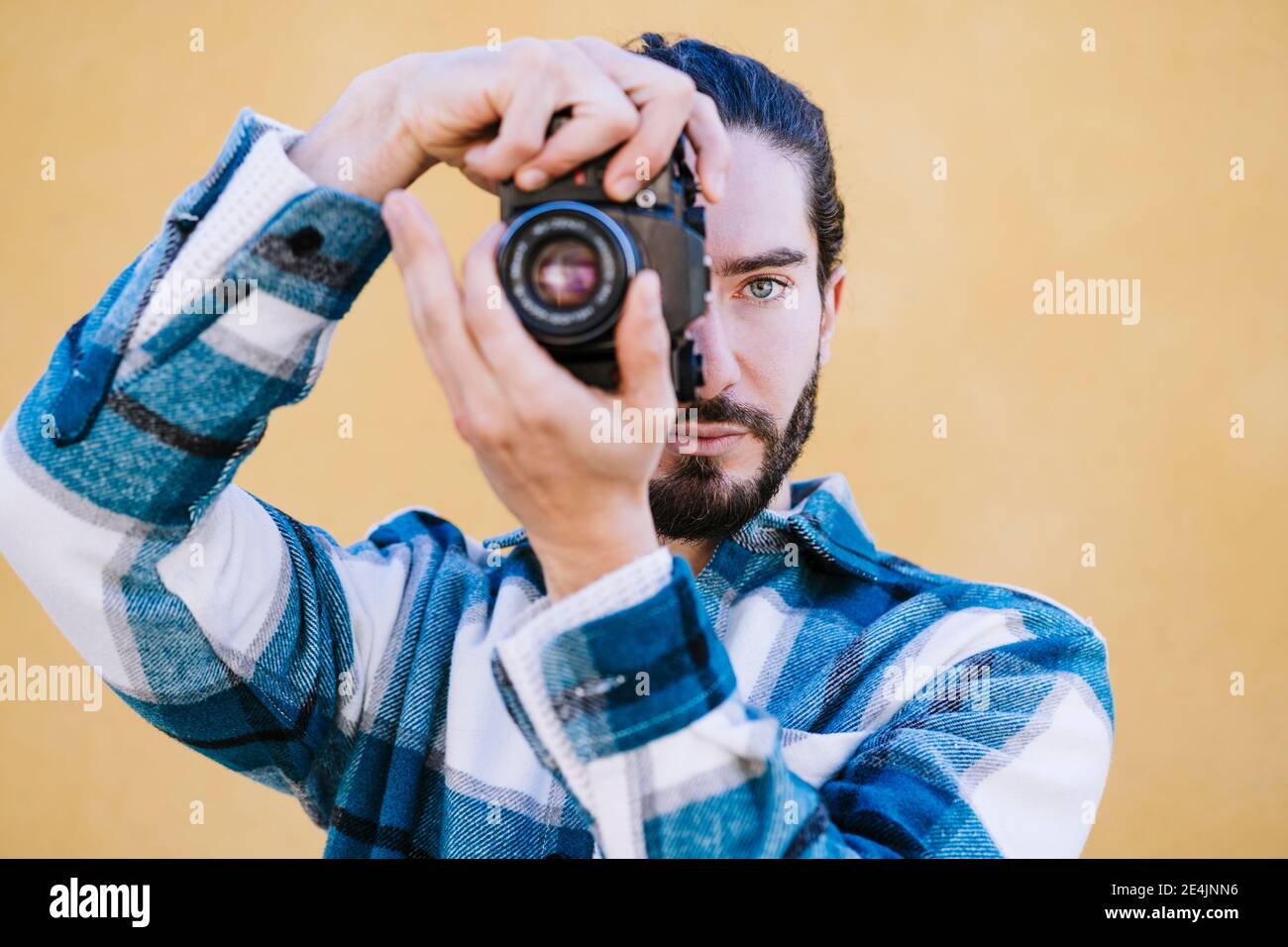 Young man photographing through camera while standing against yellow ...