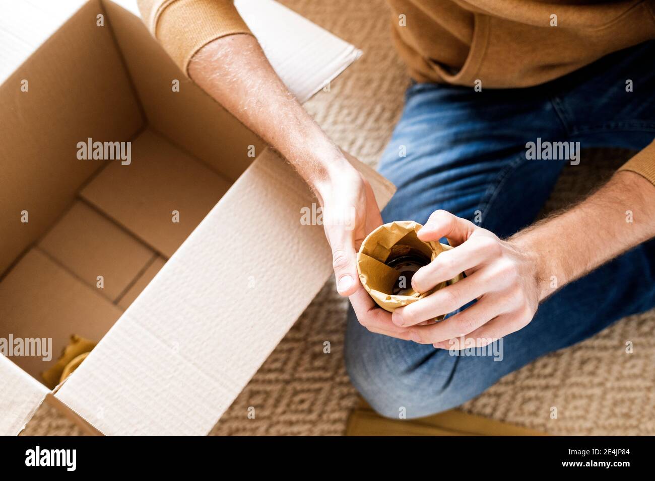 Young man keeping wrapped drinking glass in cardboard box while moving ...