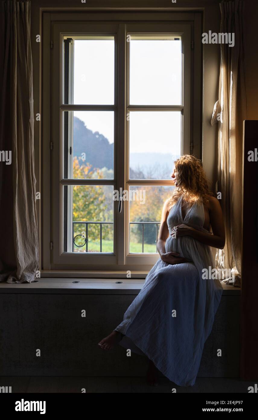 Pregnant woman sitting on window seat at home Stock Photo - Alamy