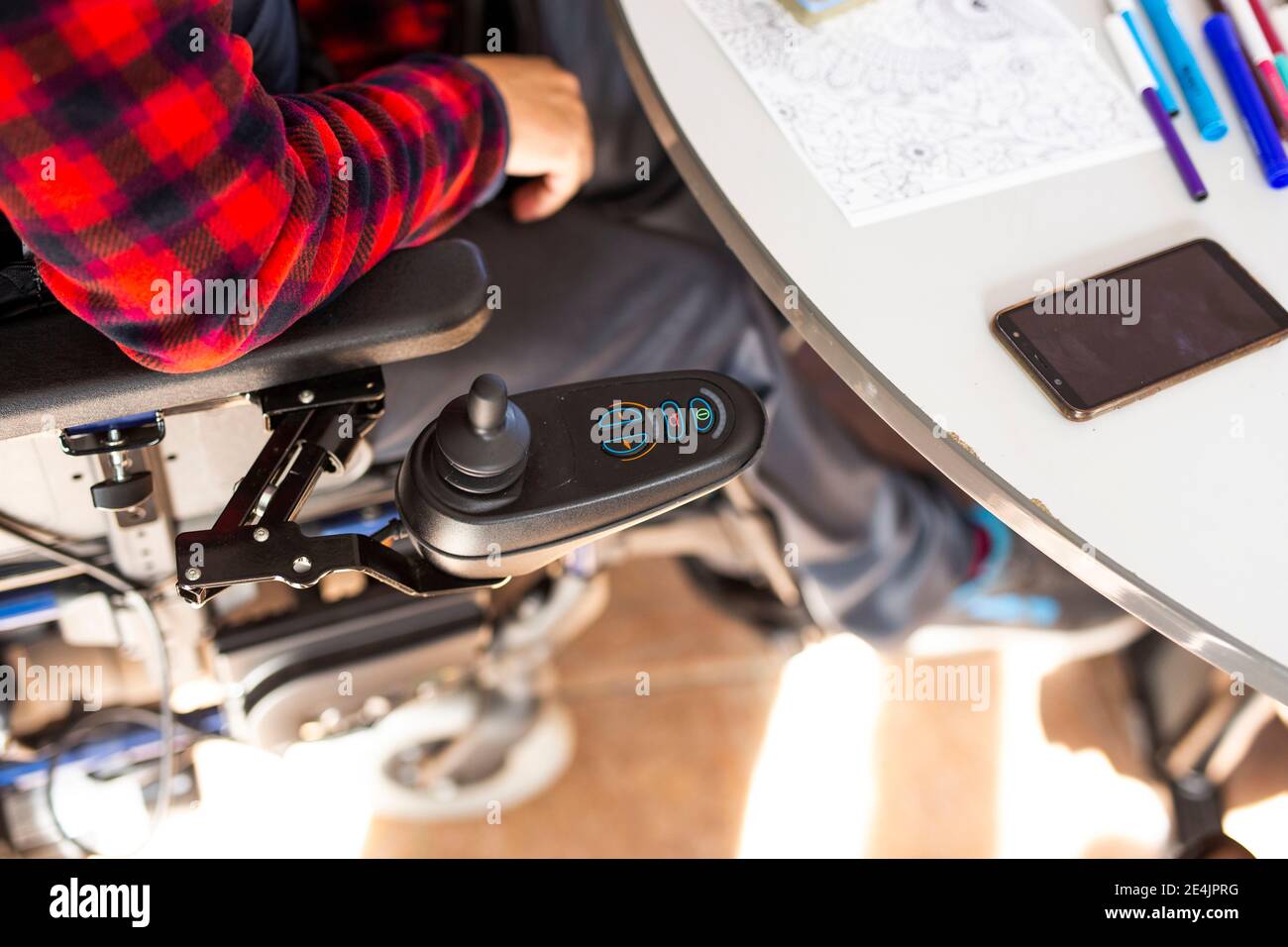 Disabled man sitting on motorized wheelchair at table in rehabilitation ...