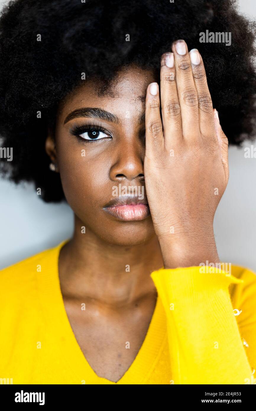 Young woman covering eye with hand while staring against white ...