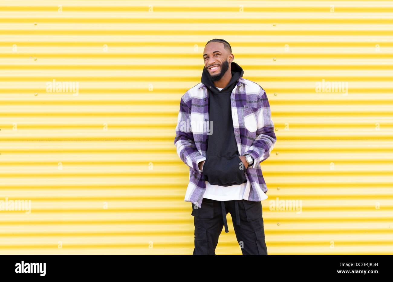 Cheerful young male rapper with hands in pockets against yellow ...