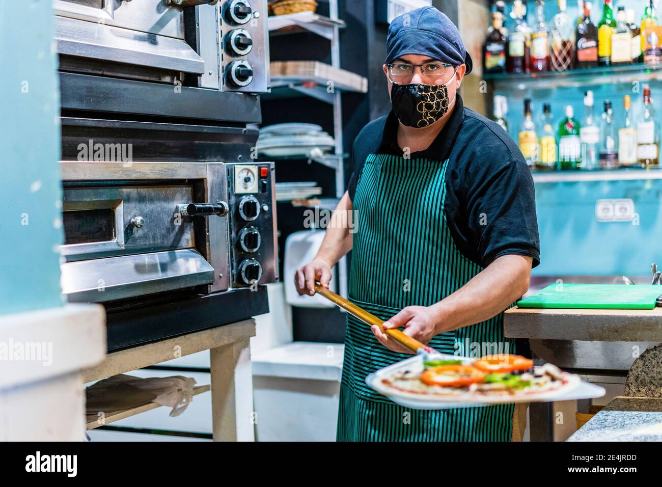 Portrait of male chef wearing protective face mask holding peel with ...