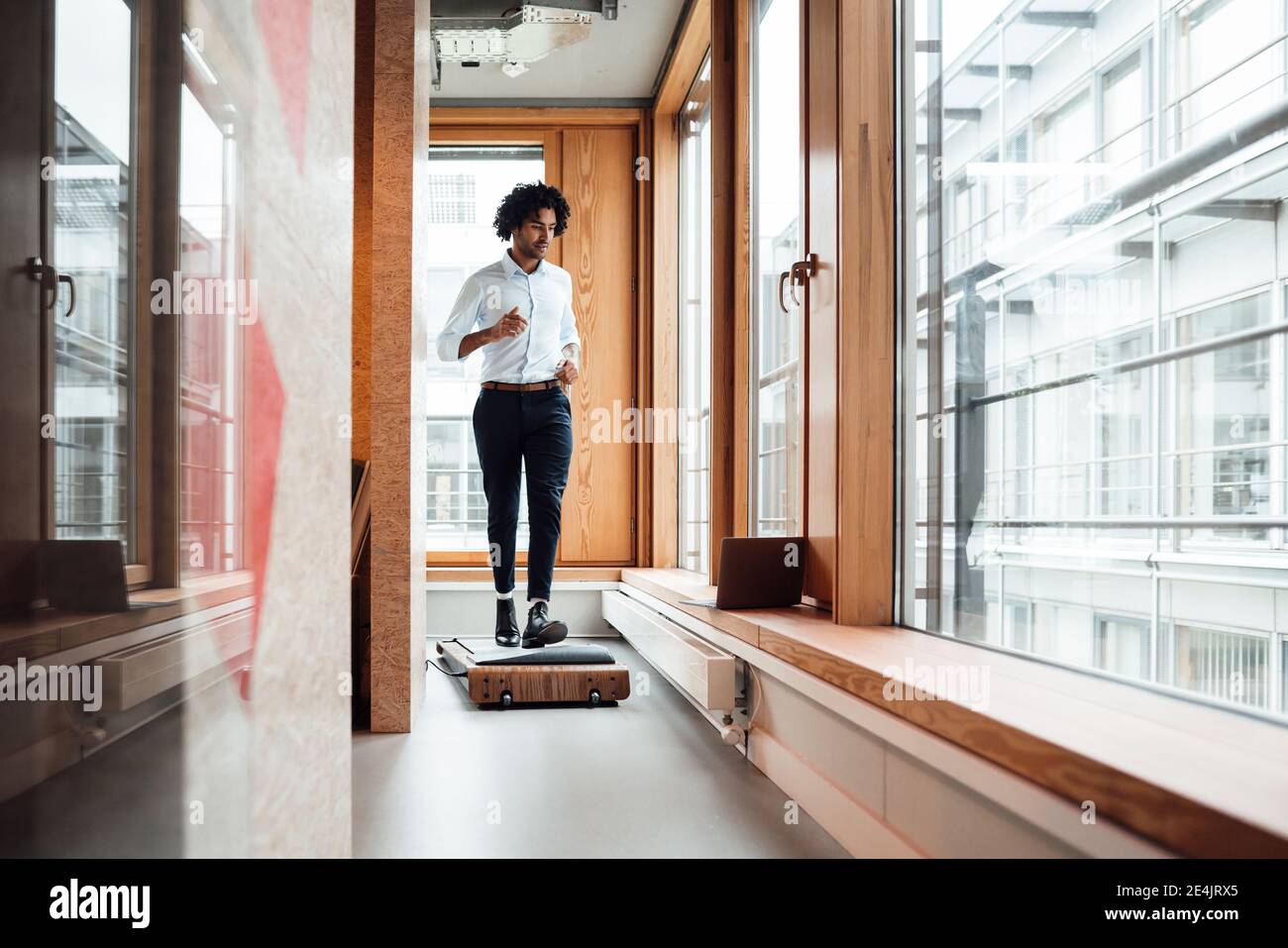 Active young businessman jogging on treadmill against window in ...