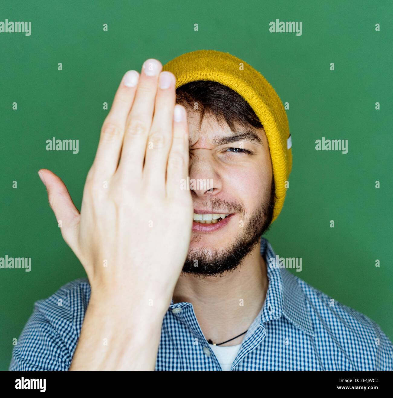 Man hiding face with hand while standing against green background Stock ...