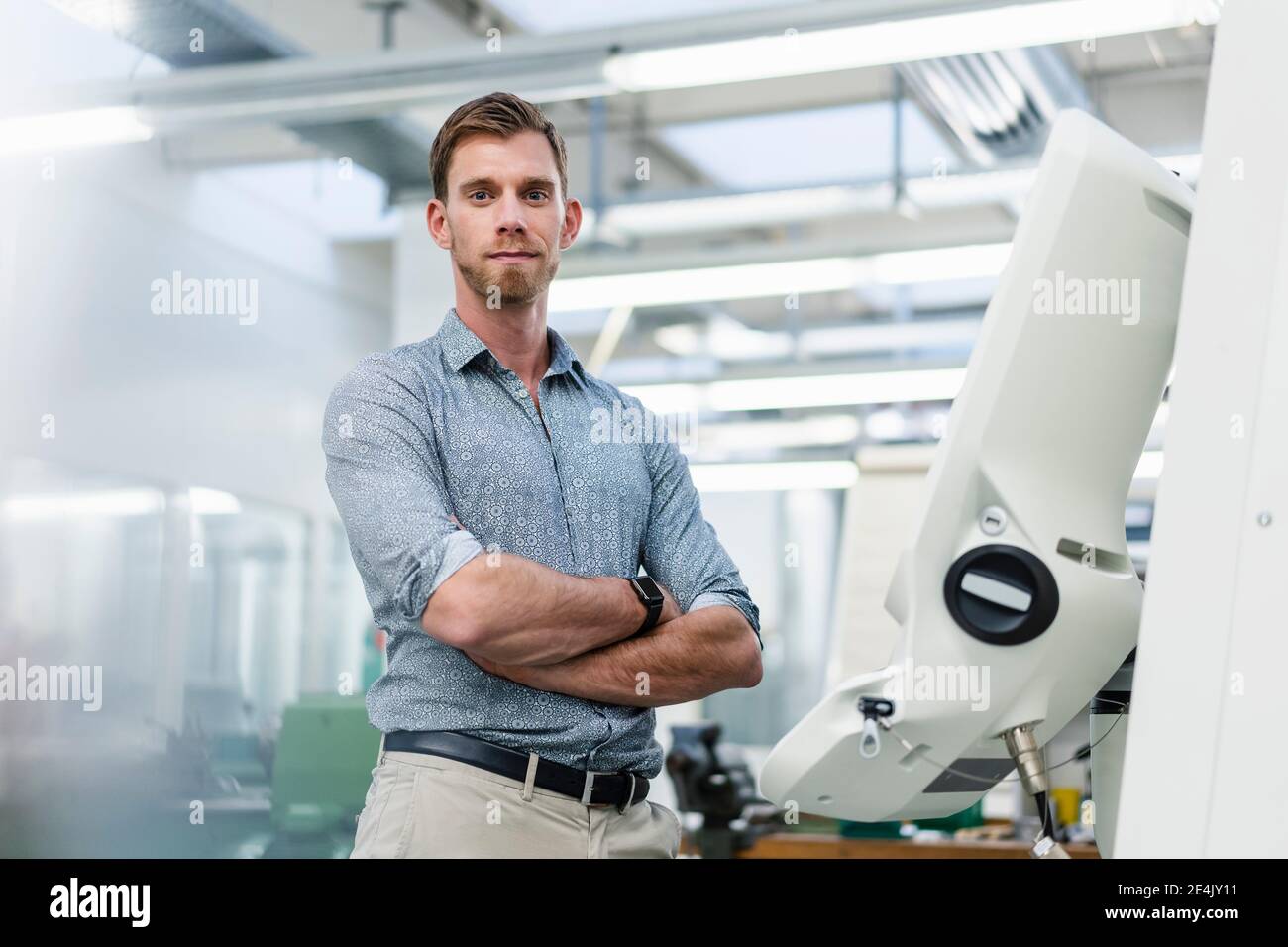 Confident male engineer with arms crossed standing by manufacturing ...