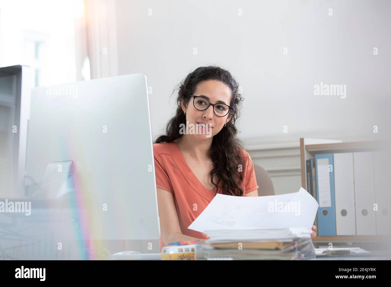 Female professional holding paper document while looking at computer in ...