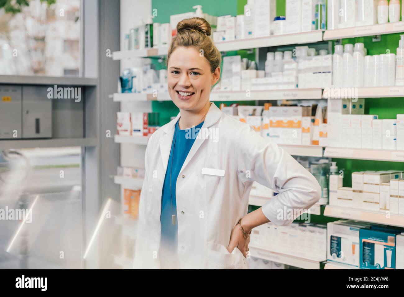 Happy pharmacist with hand on hip standing in chemist shop Stock Photo ...