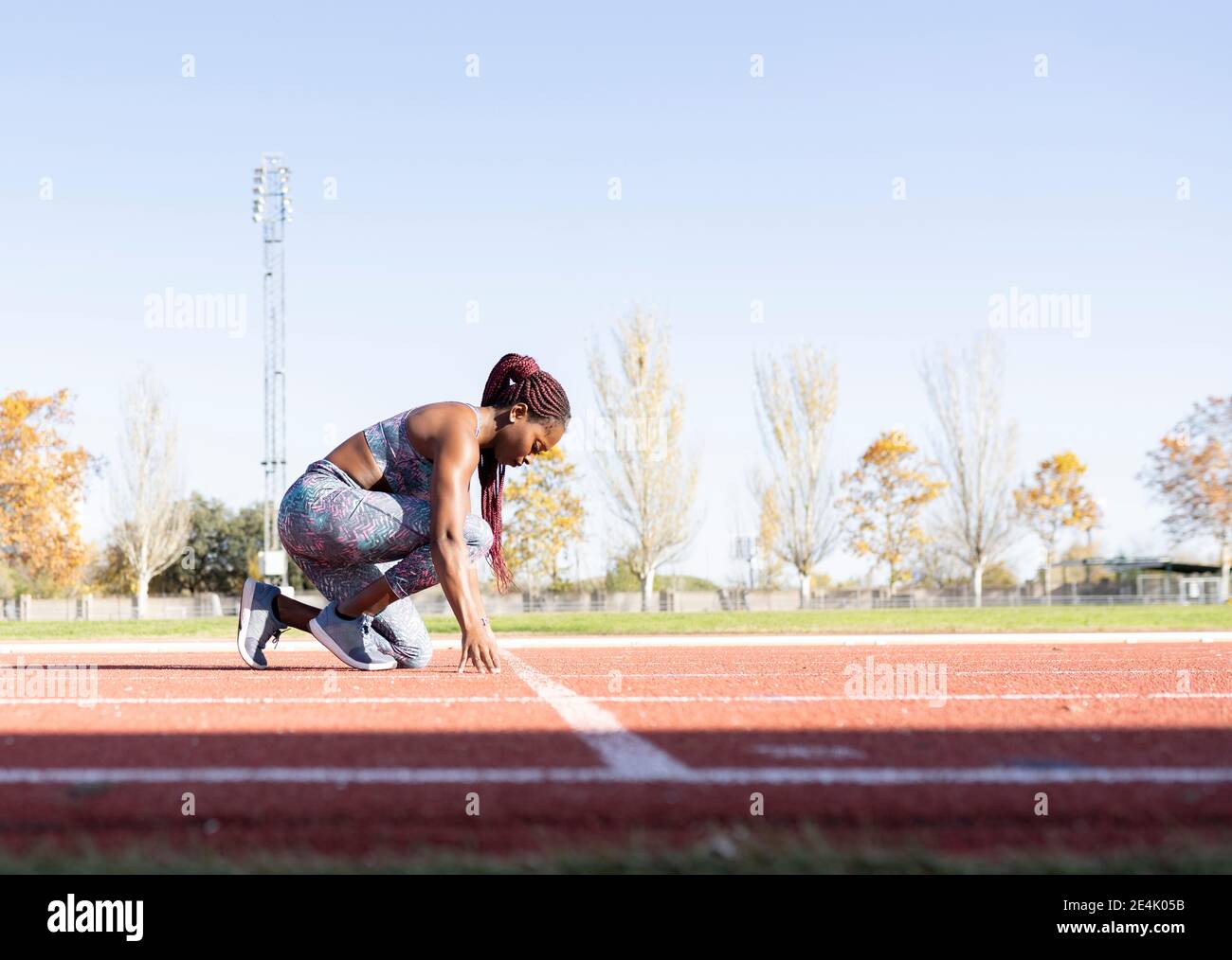 Female sportsperson in starting position on sports track during sunny ...