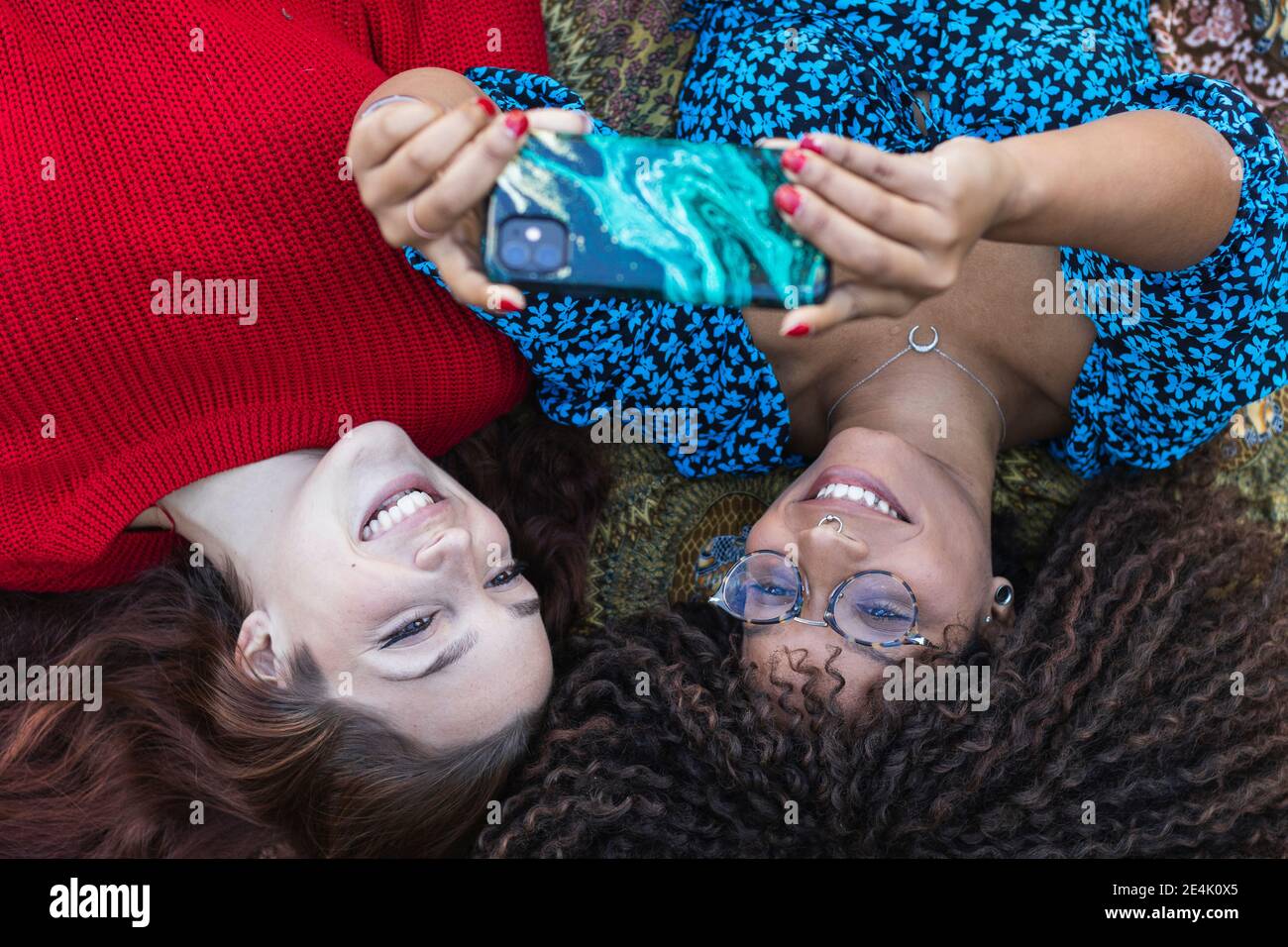 Happy young women watching mobile phone while on blanket at public park ...