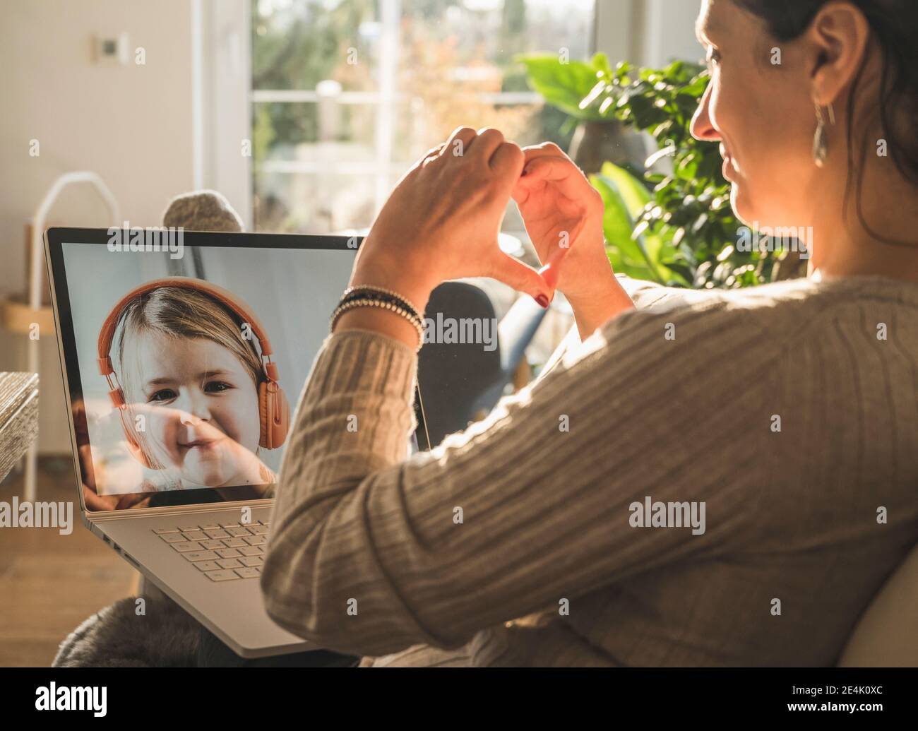 Woman making heart shape with hands during video call with little girl ...