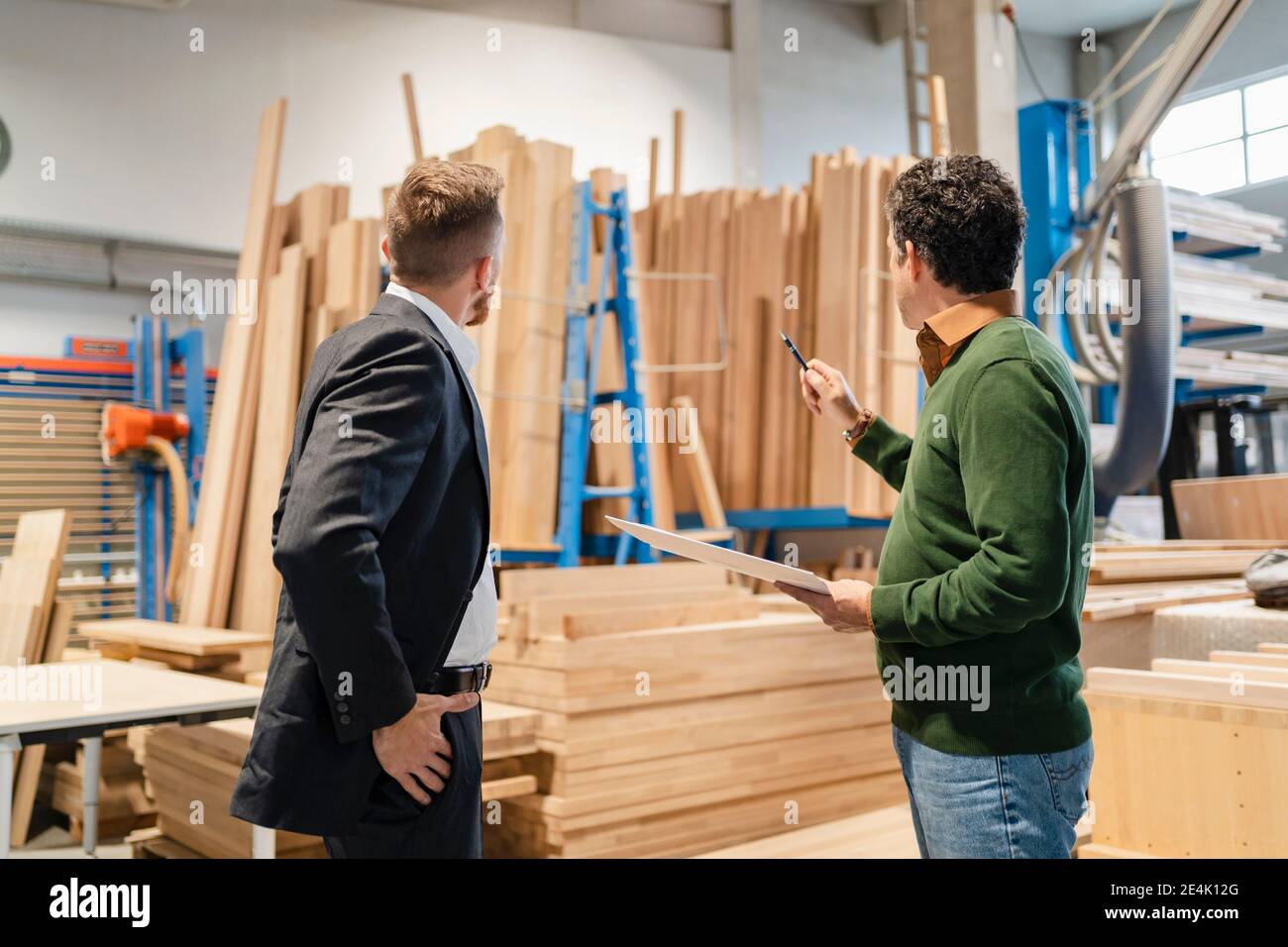 Two carpenters talking in front of stacked wood planks in production ...