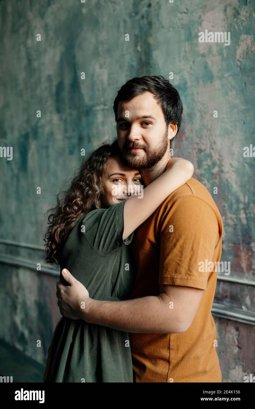 Young couple hugging while standing against wall Stock Photo - Alamy