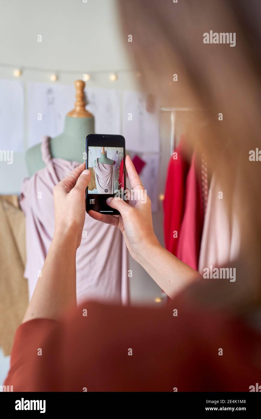 Female fashion designer photographing dressmaker's model at clothing ...