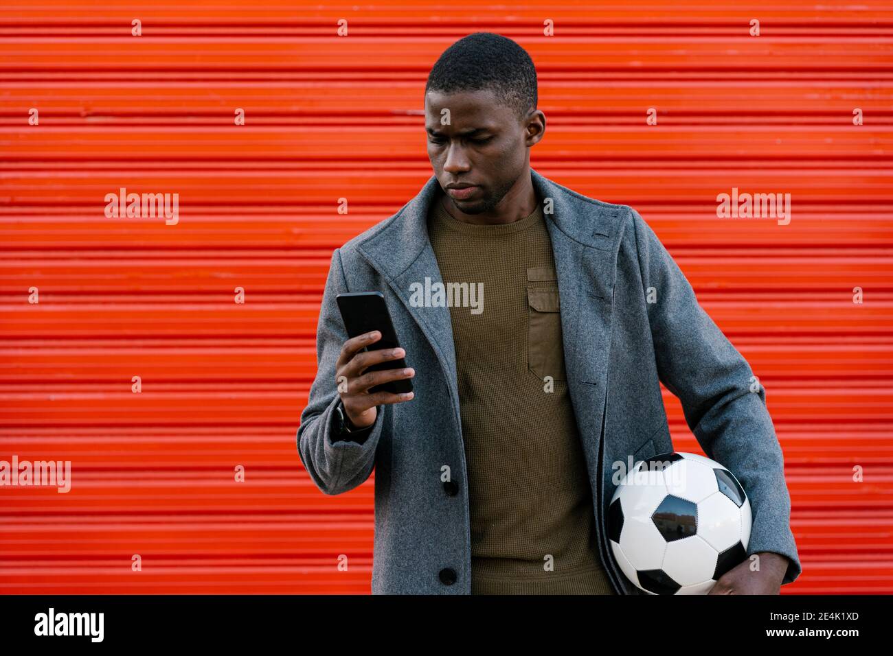 Young man with soccer ball using mobile phone while standing against ...