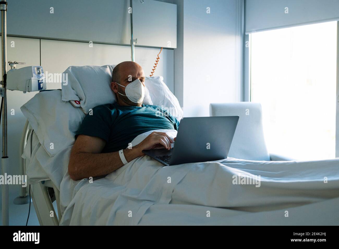 Patient holding mobile phone with IV drip hand lying on bed in hospital ...