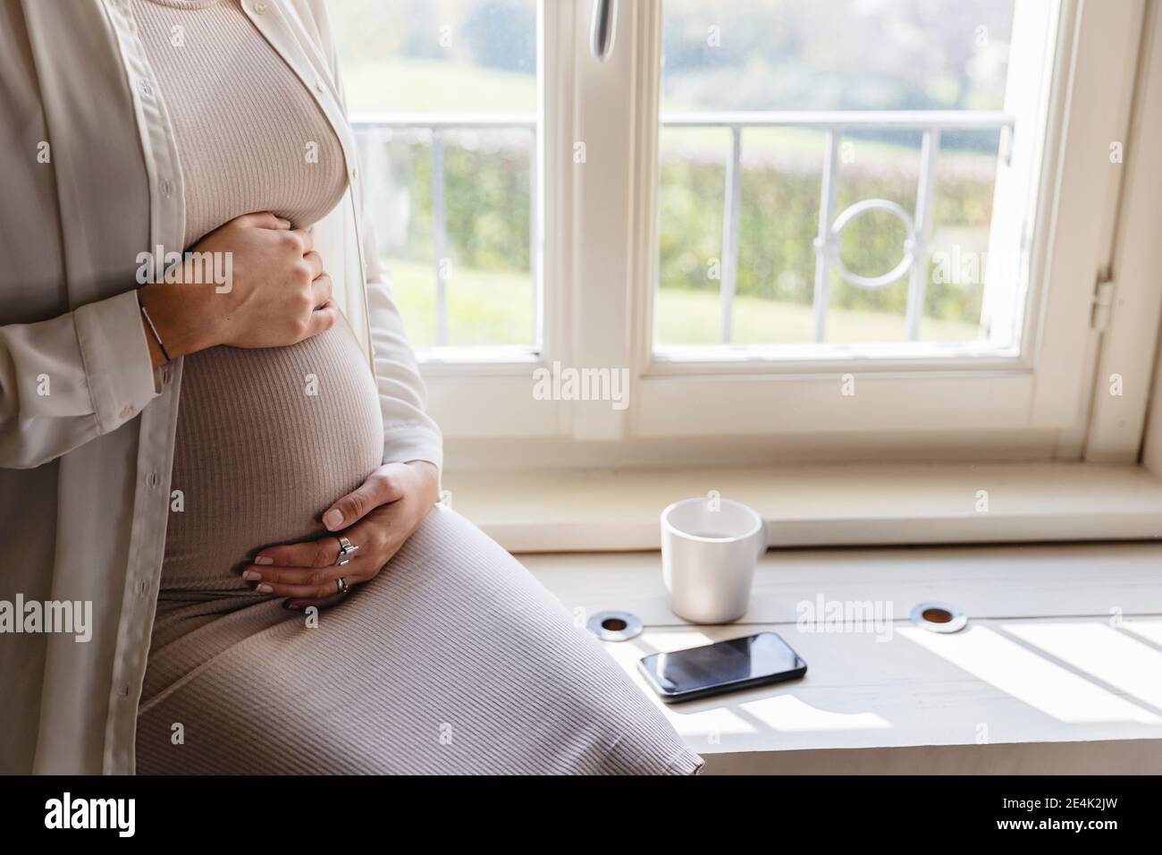 Pregnant woman hands on stomach sitting by window at home Stock Photo ...