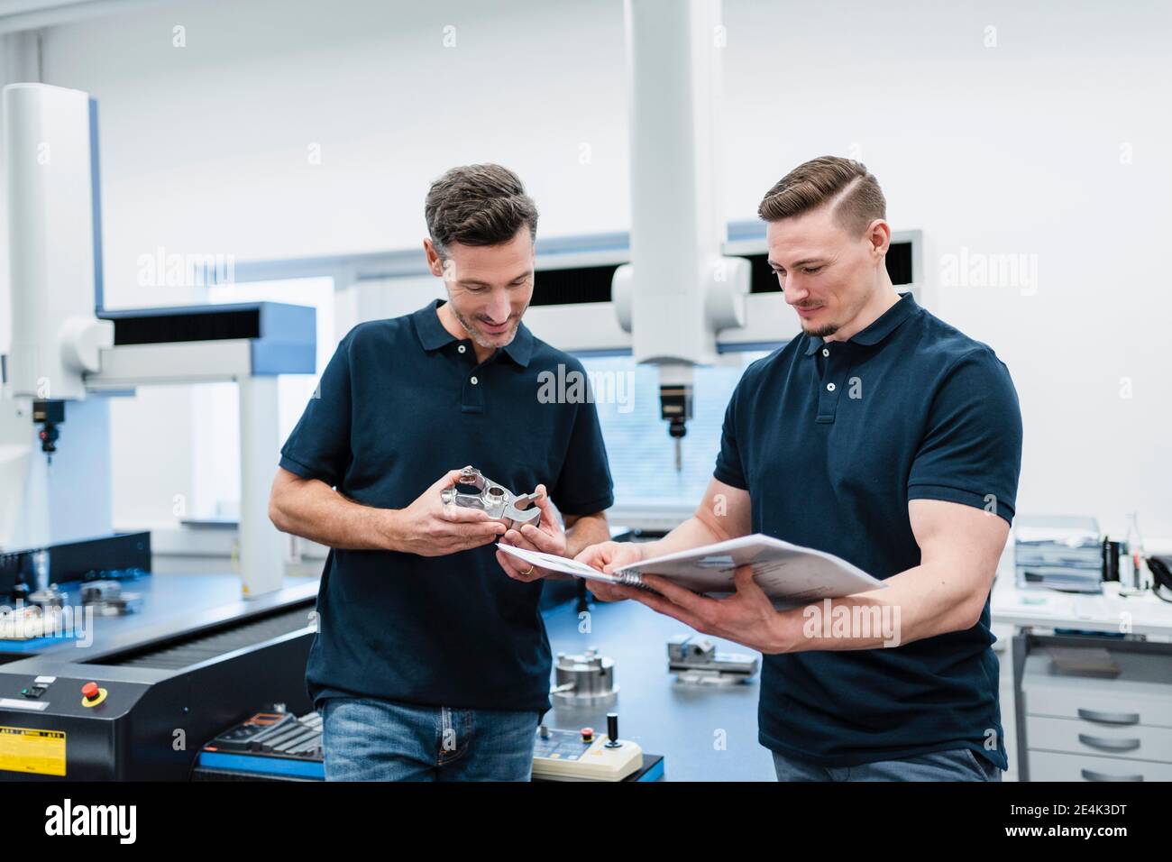 Male technicians with machine part reading instruction manual in ...