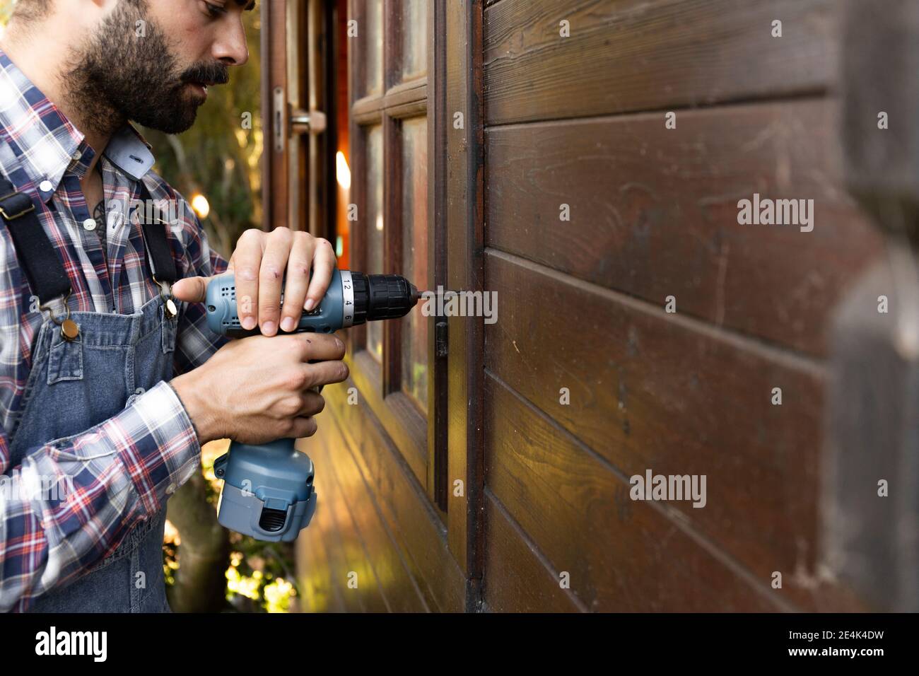 Young man using drill machine on wood house Stock Photo - Alamy