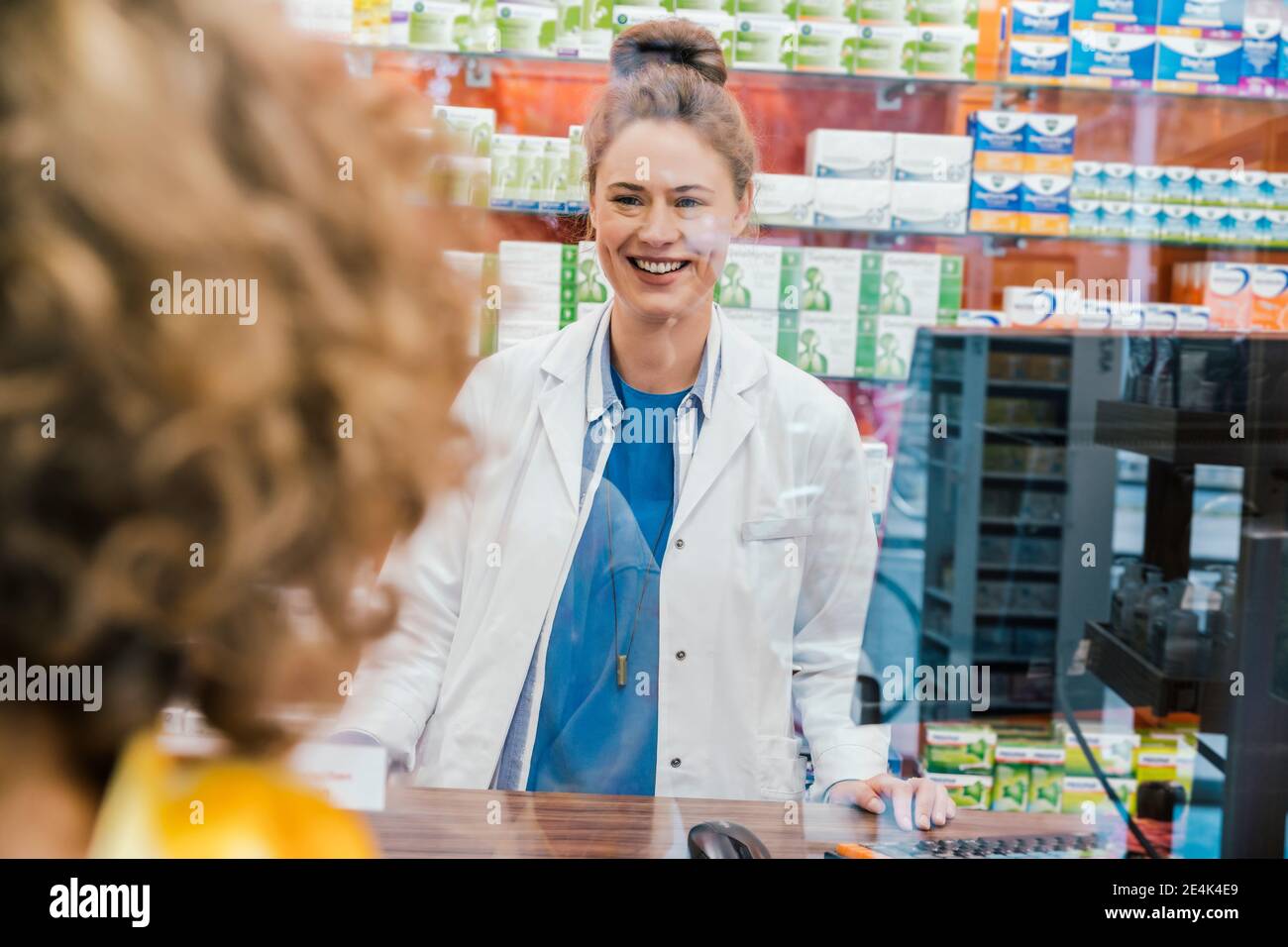 Pharmacist working at checkout counter in chemist shop talking to ...
