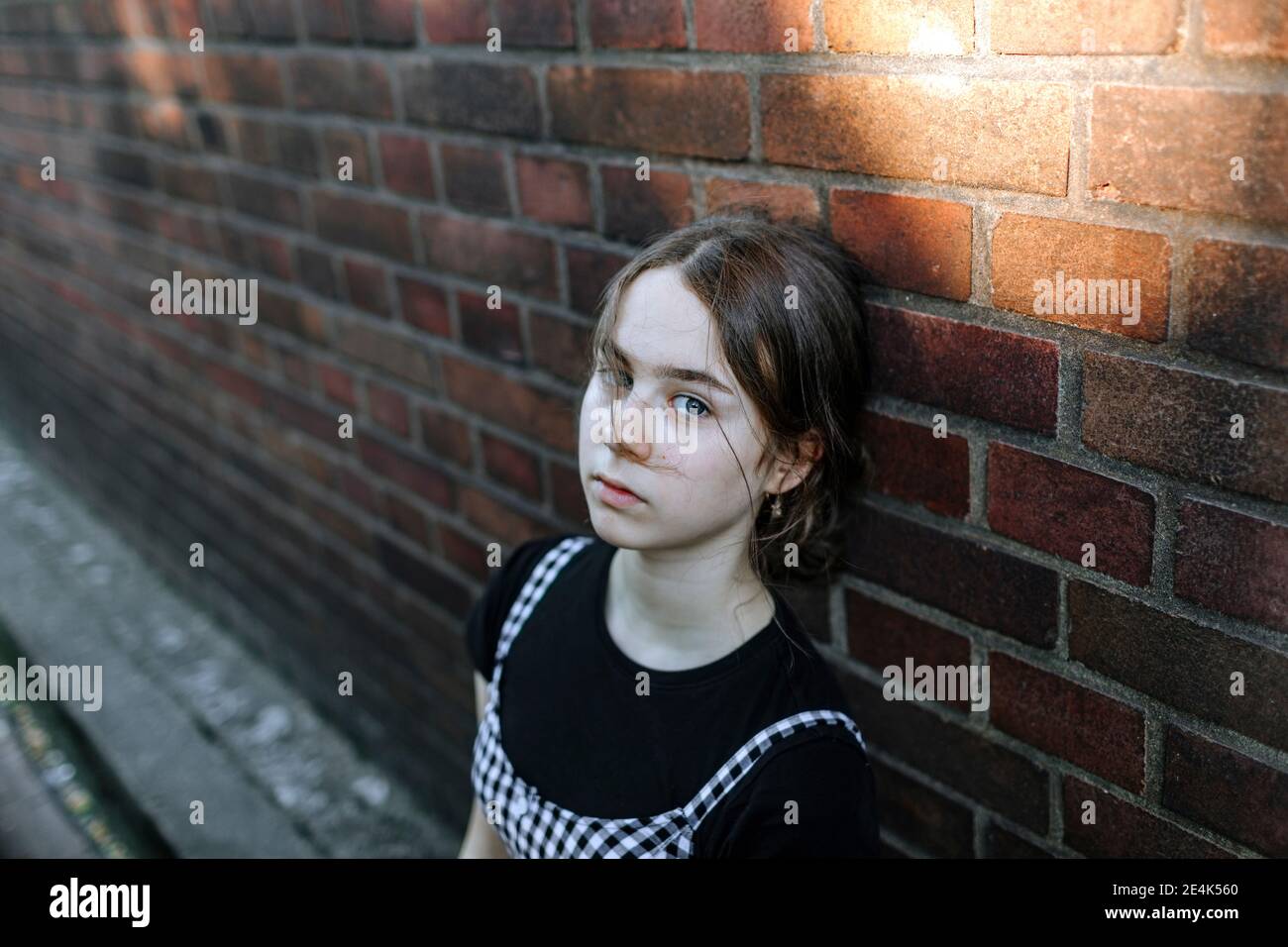 Serious teenage girl with blue eyes leaning on brick wall in city Stock ...