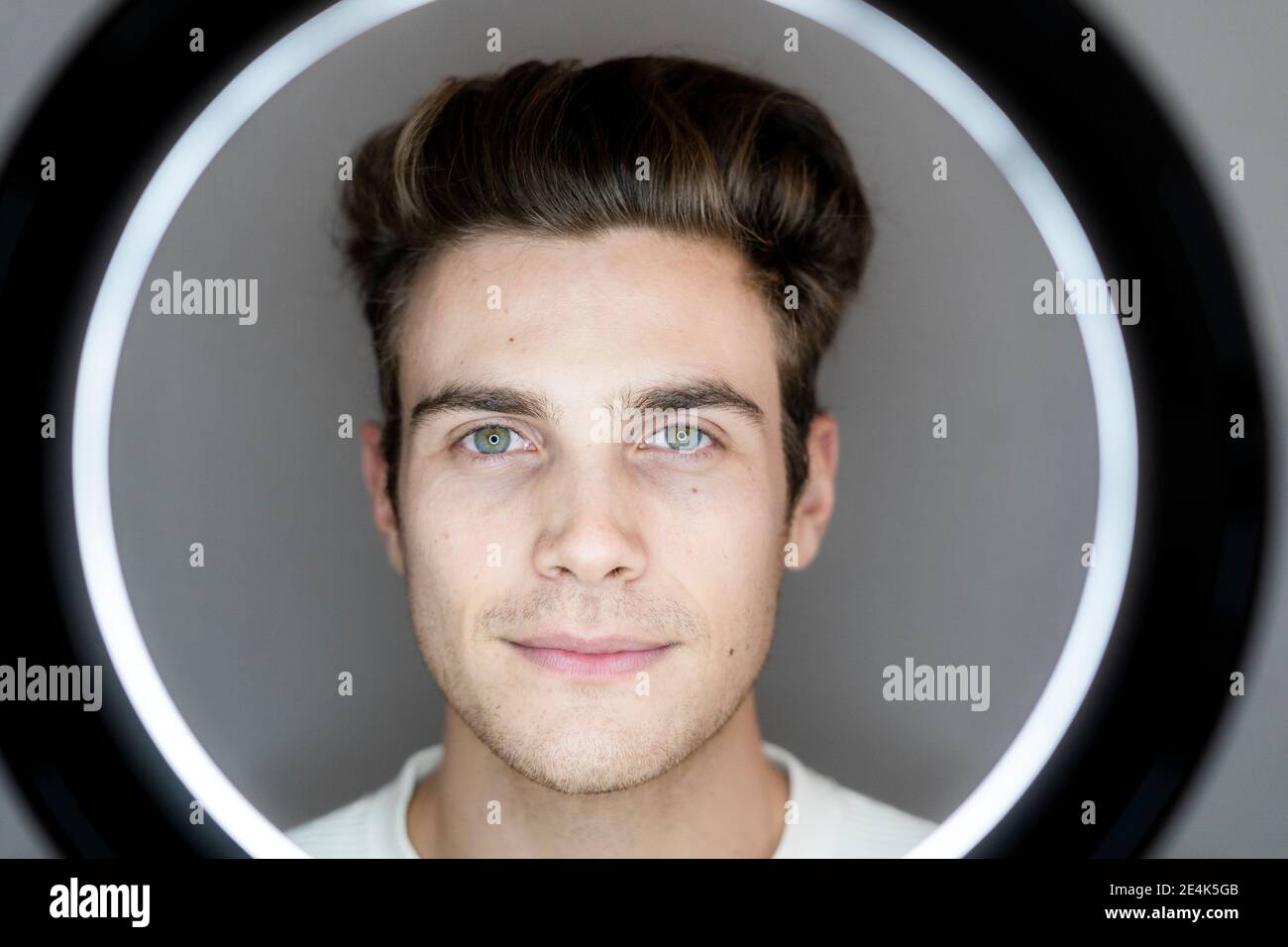 Young male influencer seen through circle light against gray background ...