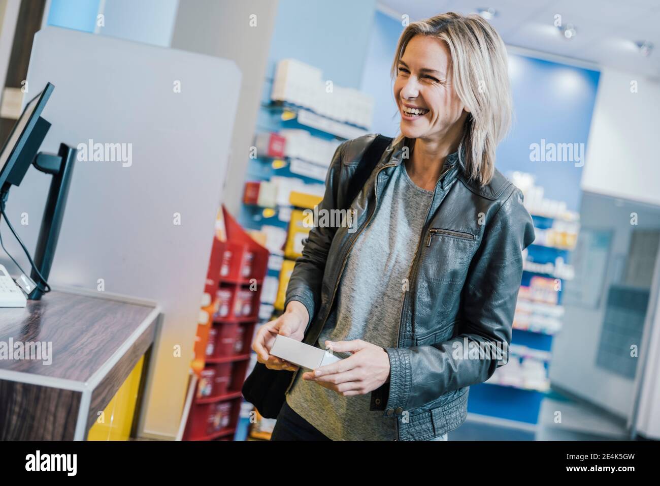 Smiling female customer with medicine standing at checkout counter in ...