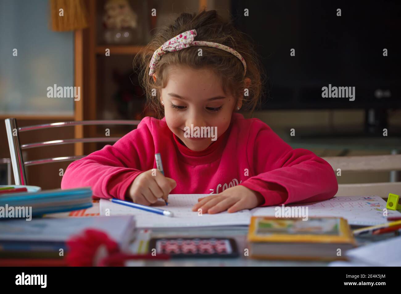 Smiling 6 year old girl does her homework, on the table the case with ...