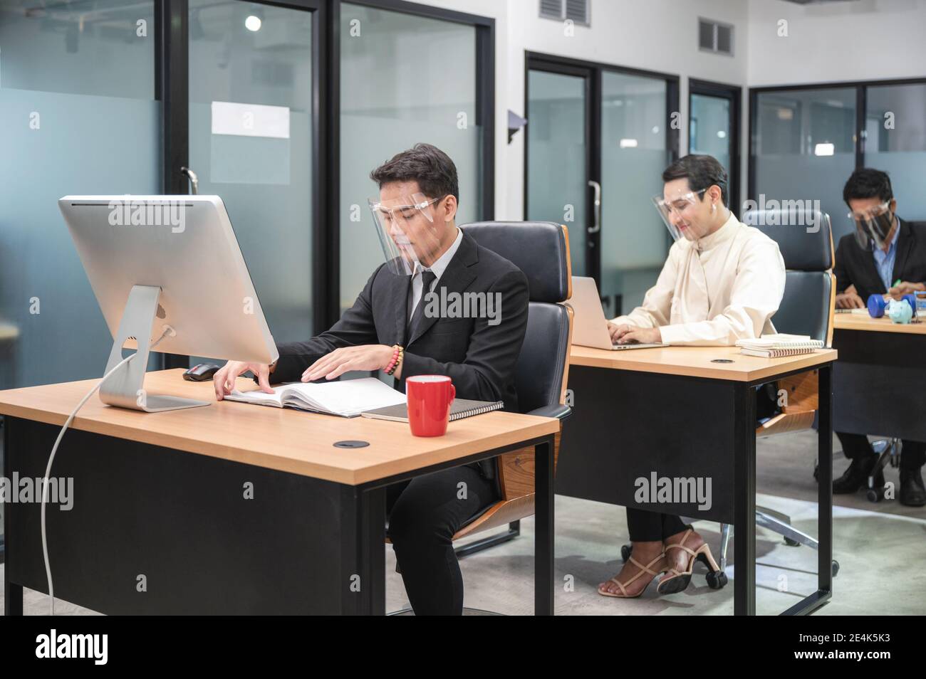 Asian employee wearing face shield working on wooden desk with desktop ...