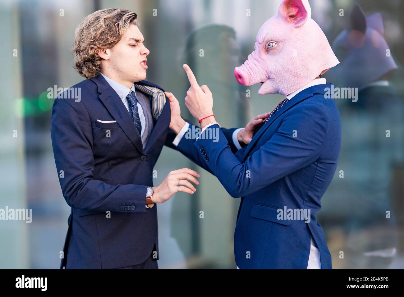 Young business holding collar of male colleague in pig mask while ...