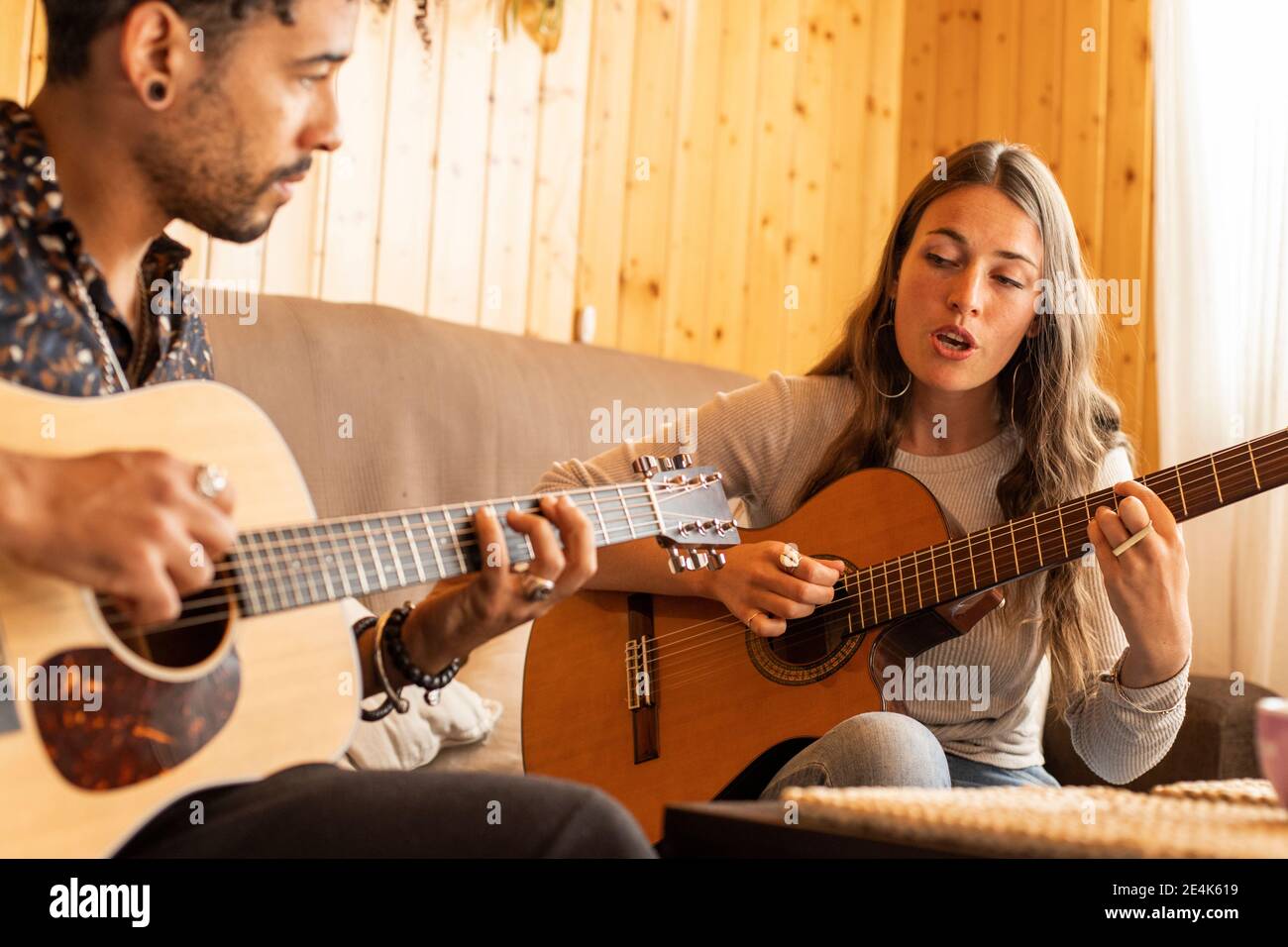 Woman singing while playing guitar with man at home Stock Photo - Alamy