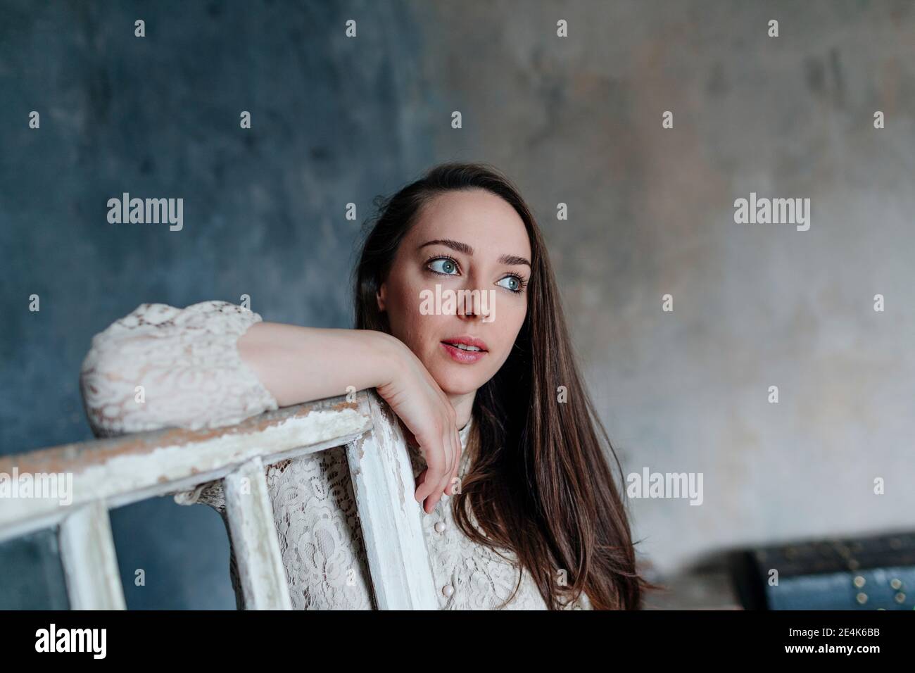 Thoughtful beautiful woman with old window frame standing against wall ...