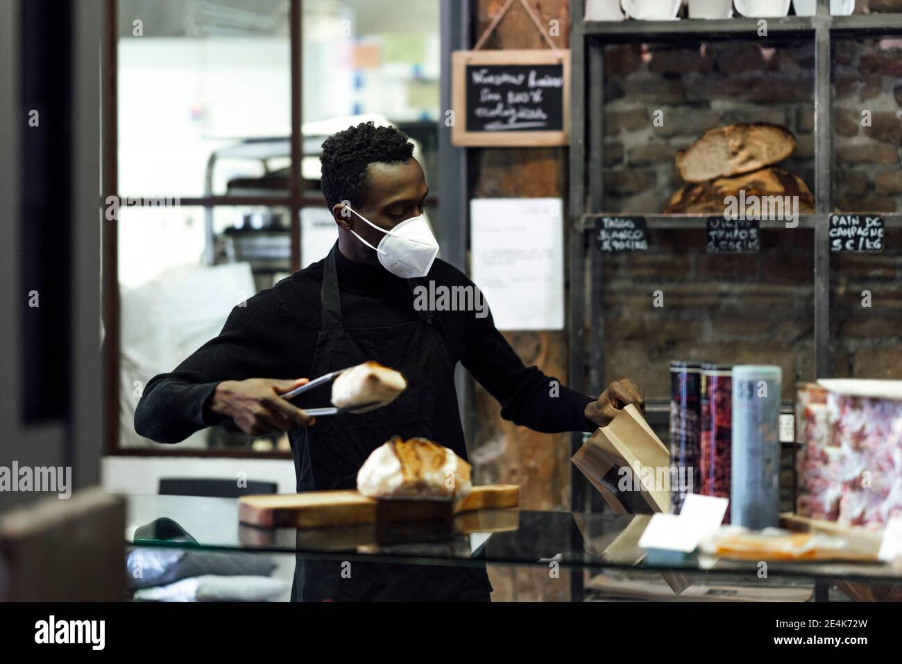 Salesman wearing face mask packing bread while standing at bakery Stock ...