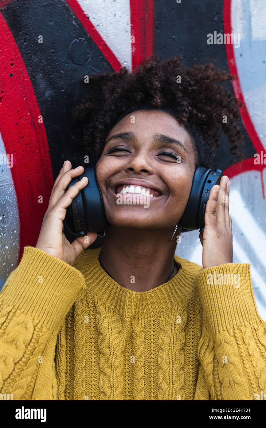 Happy young woman with eyes closed listening music through headphones ...