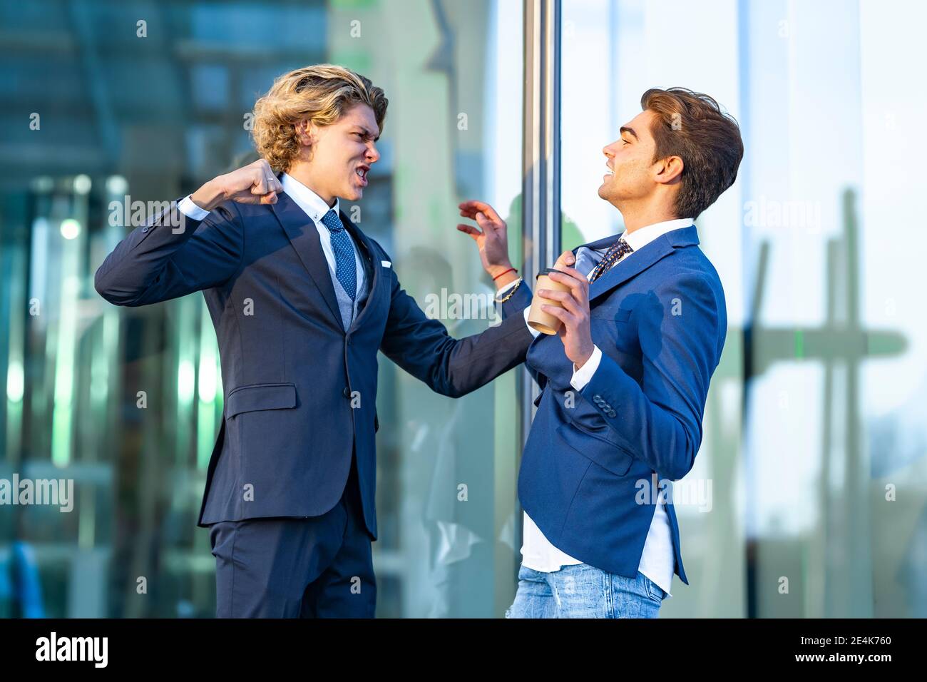 Angry young businessman fighting with male colleague outside office ...