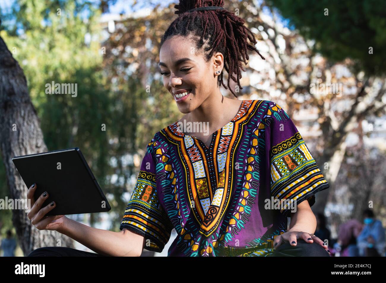 Smiling beautiful Jamaican woman with dreadlocks using digital tablet ...