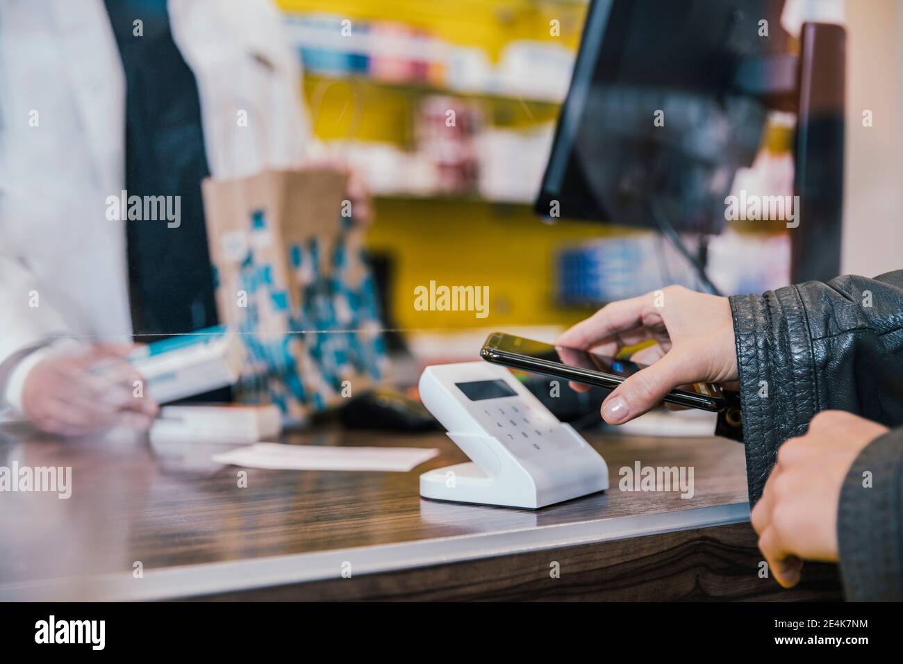 Hand of customer with mobile phone at checkout counter in chemist shop ...
