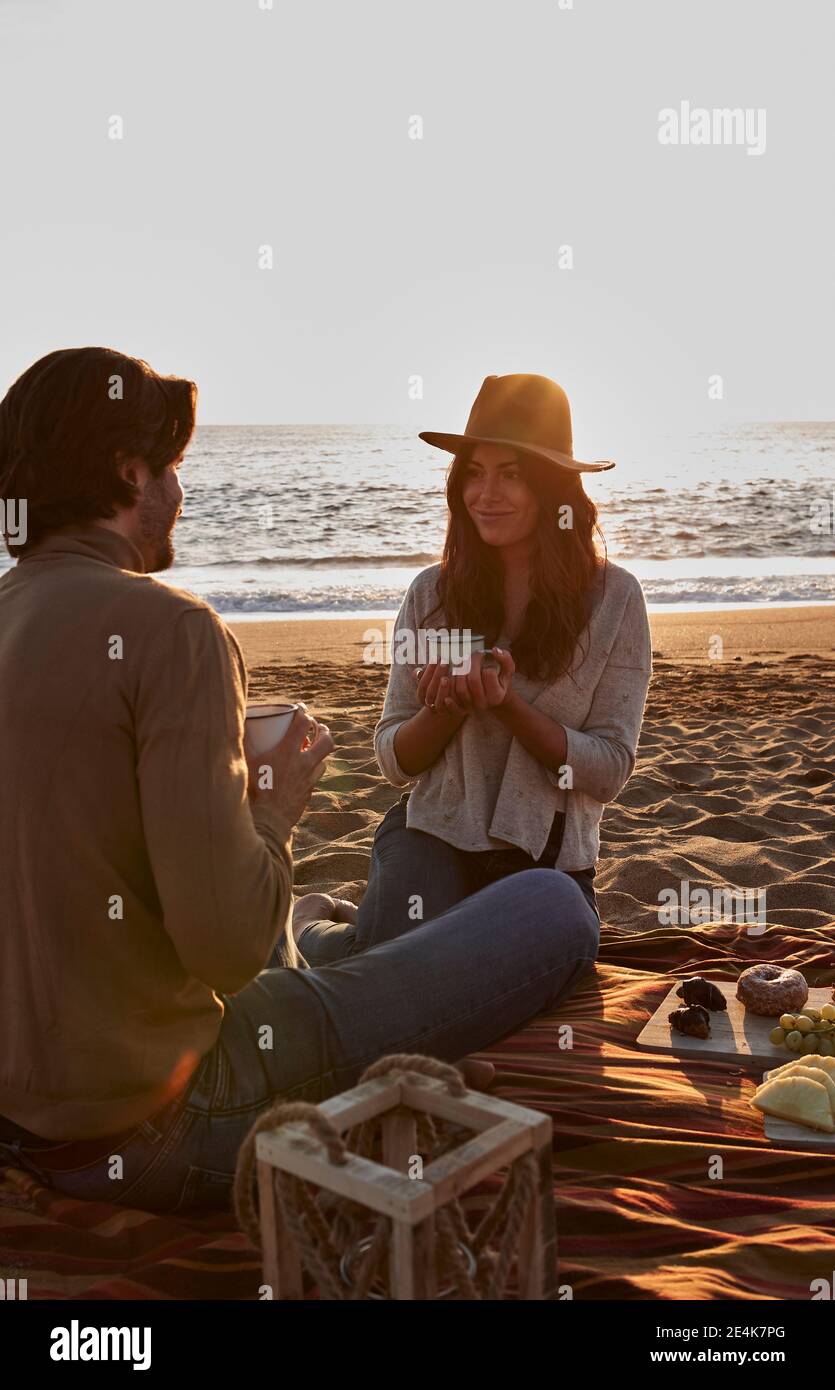 Young couple drinking coffee while sitting on beach Stock Photo - Alamy