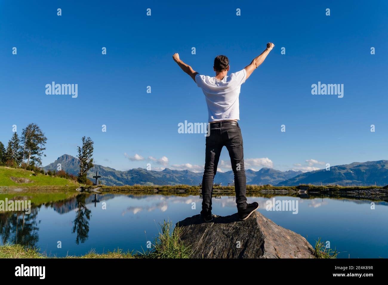Man standing with raised arms on top of lakeshore boulder Stock Photo ...