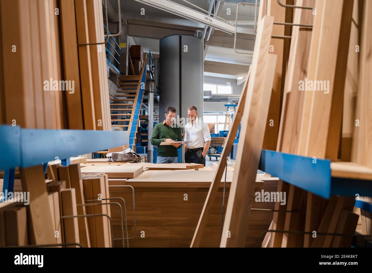 Two carpenters talking in production hall with wooden planks in ...