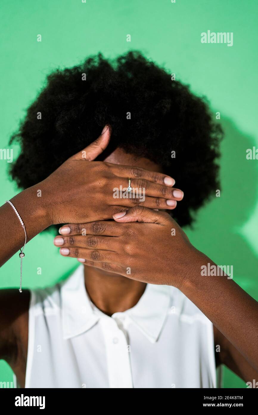 Young woman hiding face with hand while standing against green ...