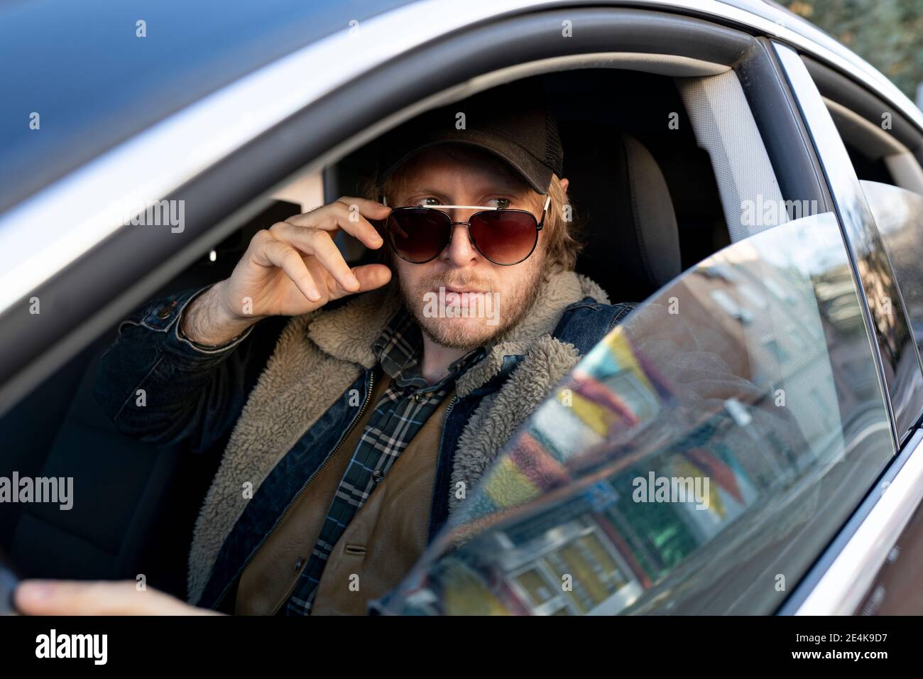 Man wearing sunglasses looking away while sitting in car seen through ...