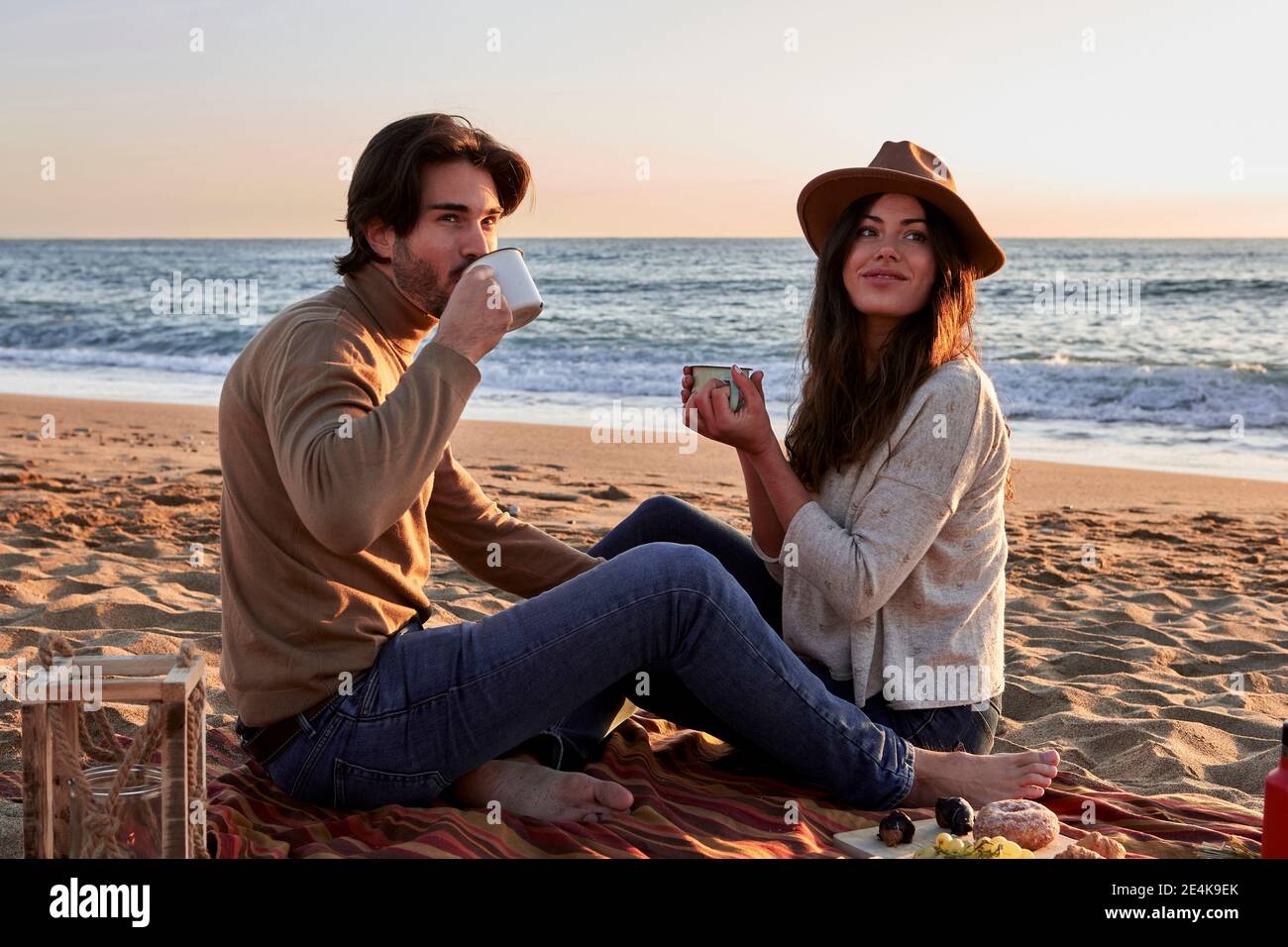 Young couple drinking coffee while sitting together on beach Stock ...