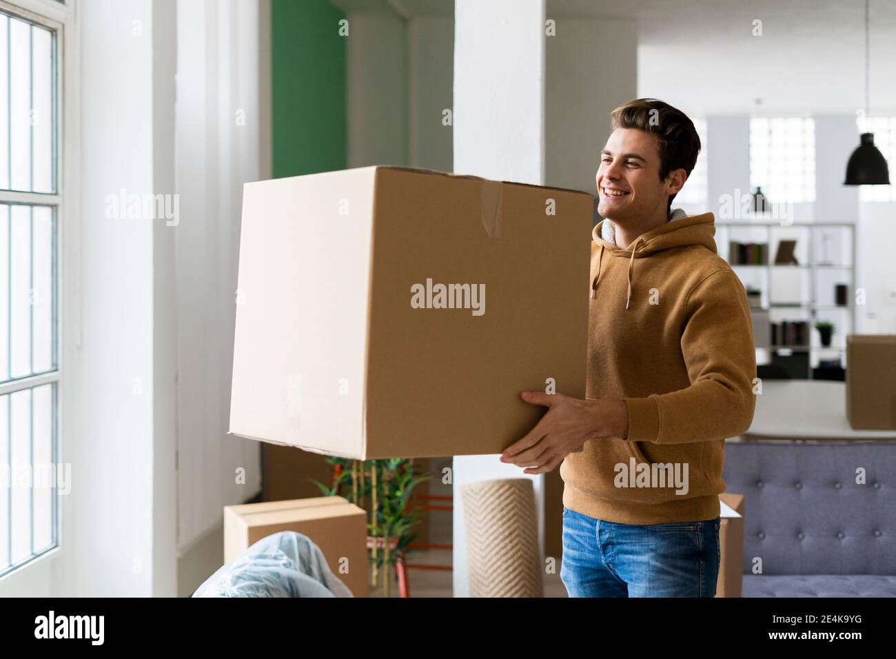 Happy young man carrying box in new loft apartment Stock Photo - Alamy