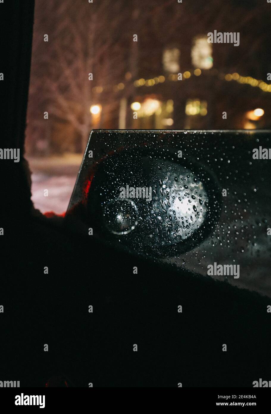 A vertical shot of a half-opened car window at night during the rain ...