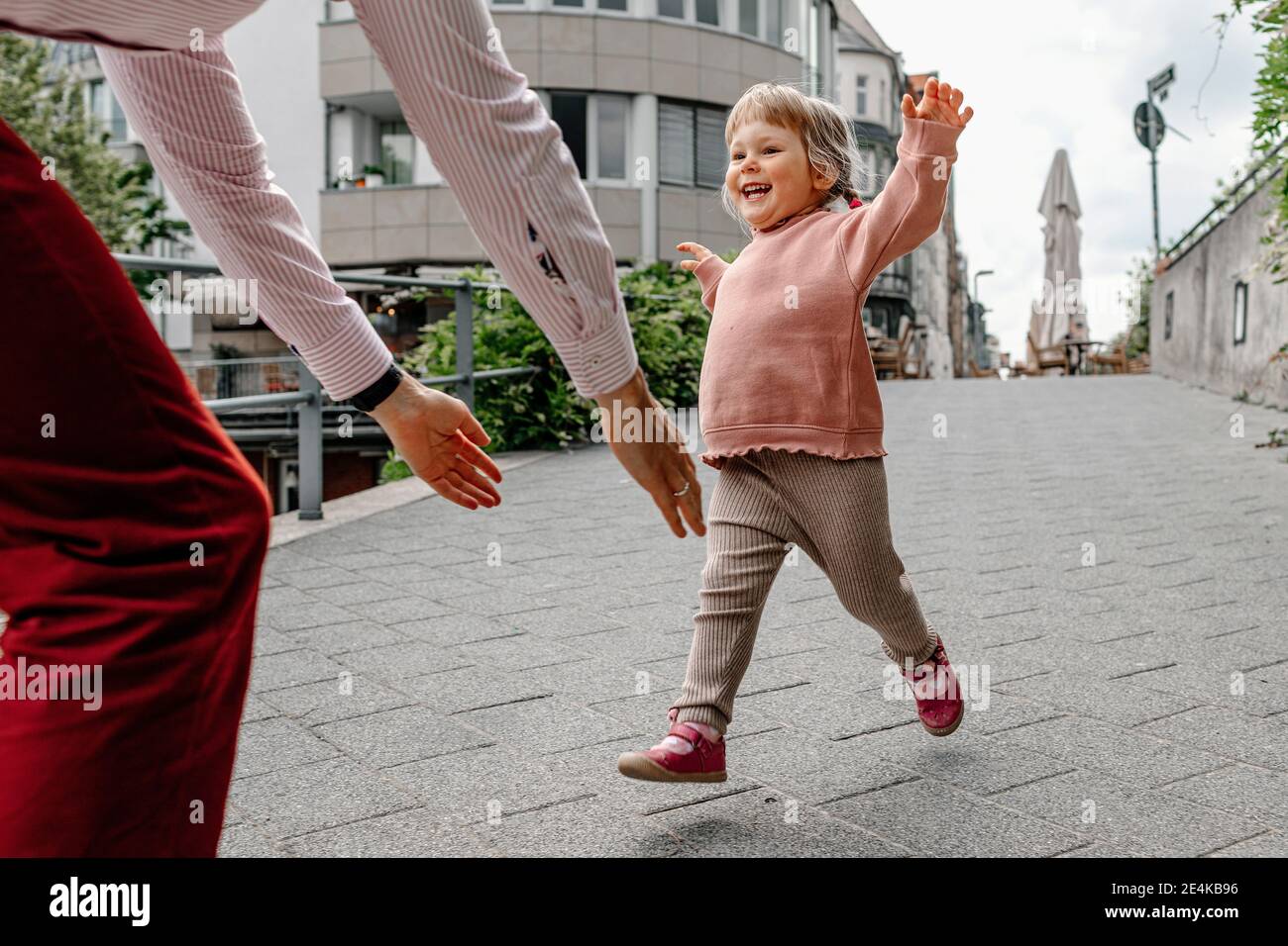 Cheerful daughter running towards her father while playing on street in ...