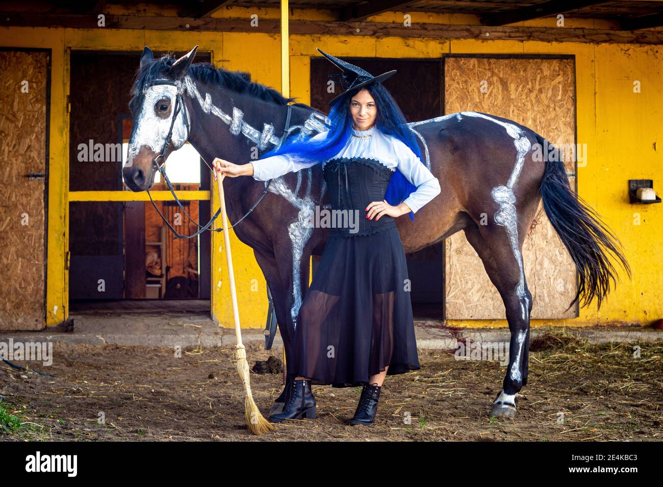 A girl dressed as a witch stands with a broom near a horse on which a ...